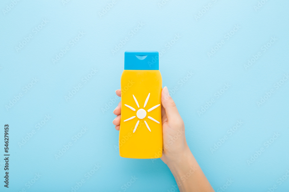Young adult woman hand holding yellow tube of sunscreen on light blue ...
