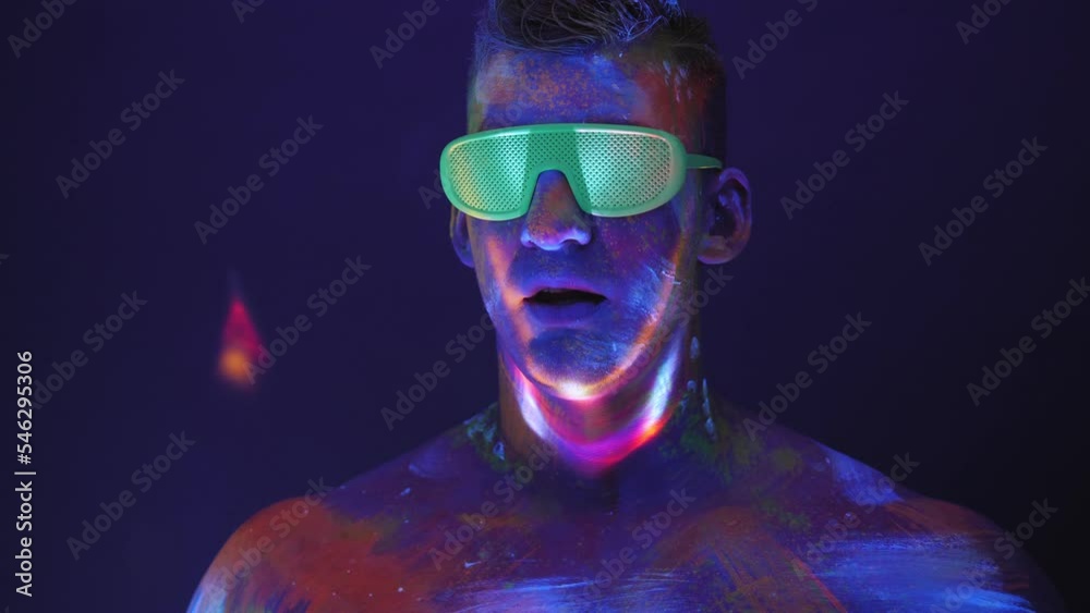 A muscular man with ultraviolet drawings on his body stands in the dark ...