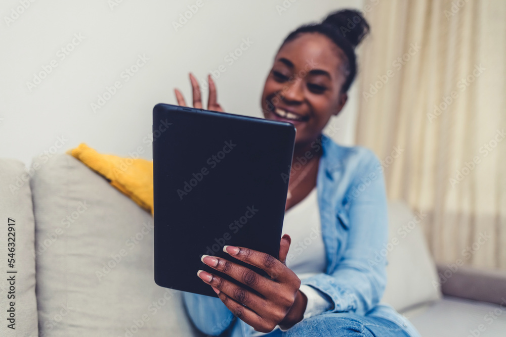 Smiling young African American woman sit on sofa at home wave greet ...