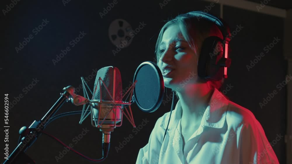 Beautiful blonde girl in headphones performs song in recording studio ...