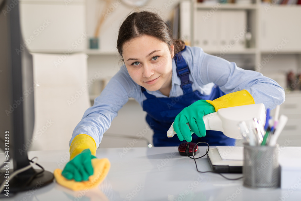 Young girl cleans up the desktop in the office with a rag and cleaning ...