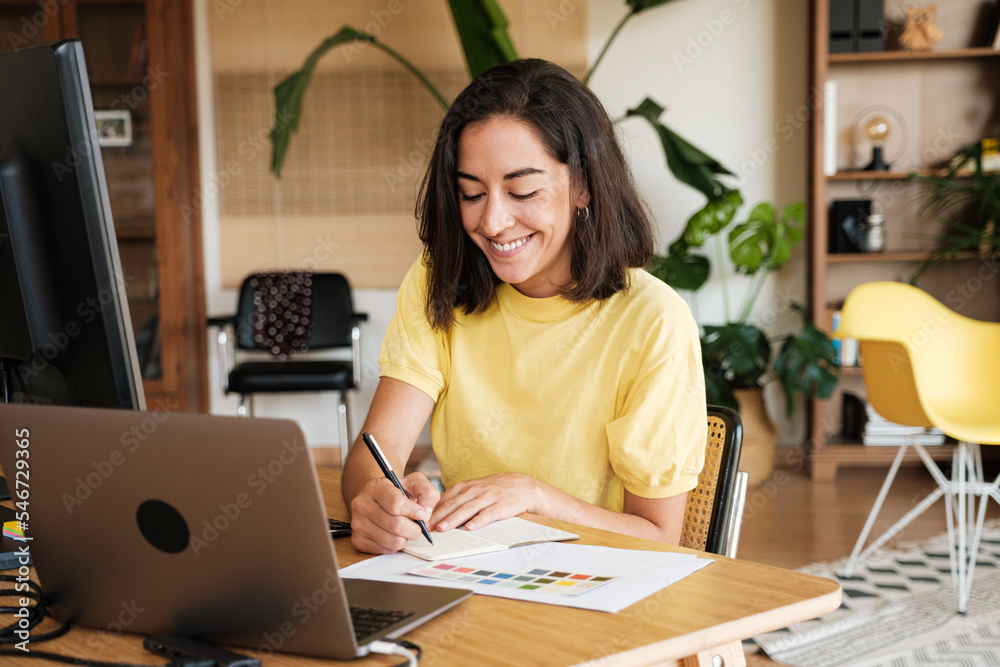 Woman taking notes while working on laptop Stock Photo | Adobe Stock