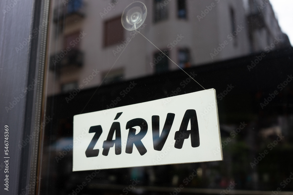 Sign in the shop window behind a pane of glass saying 'zárva' which ...
