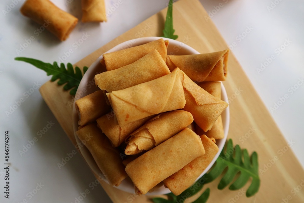 Sumpia or mini crunchy spring rolls on white plate and wooden cutting ...