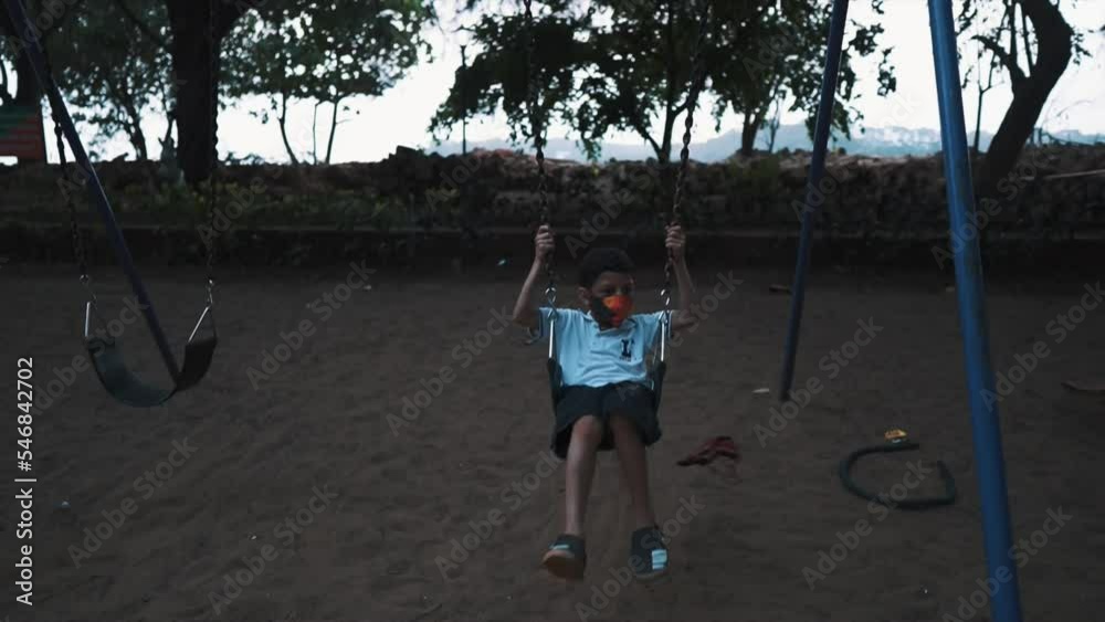 A young boy playing on a swing in a park playground, building momentum ...