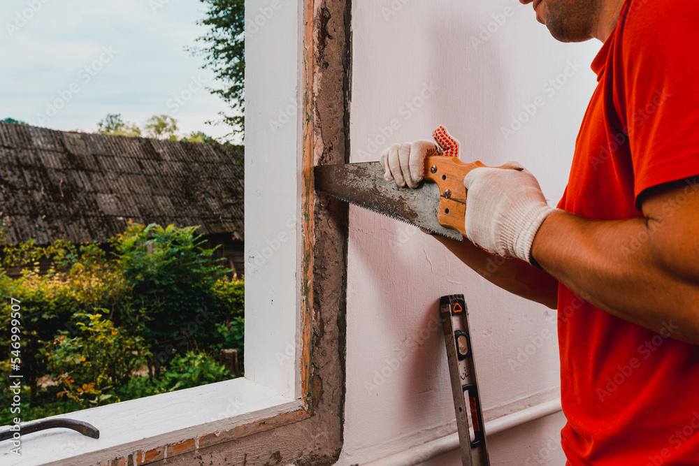 The man with a hand saw cuts the mounting wool around the window frame ...