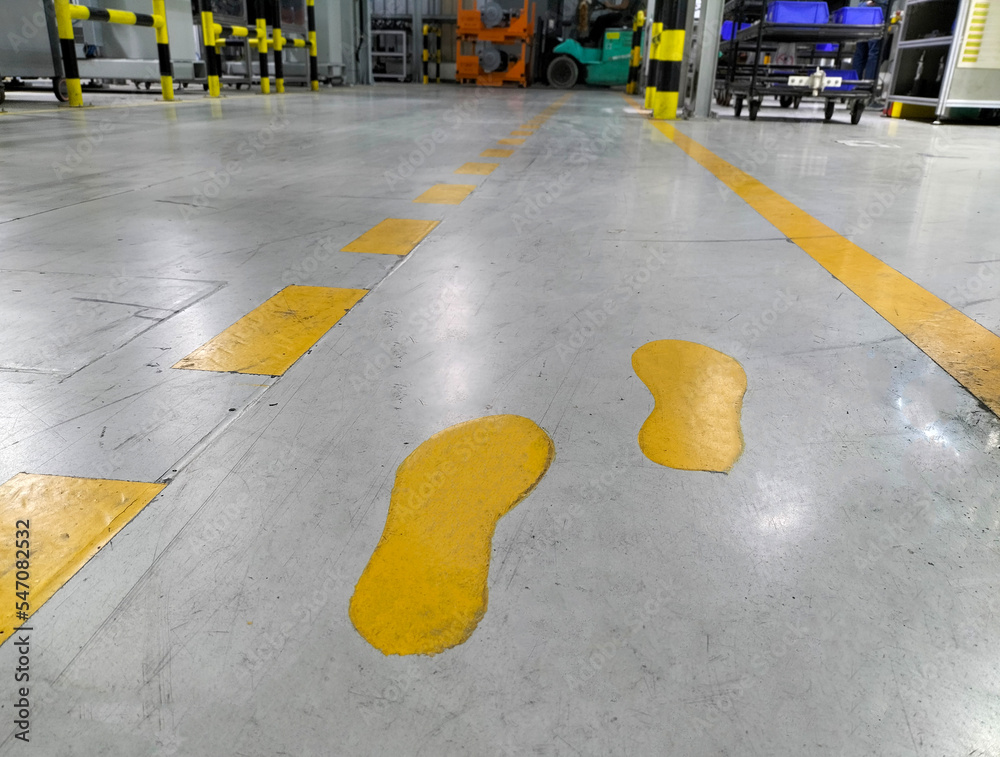 A walkway in an industrial building painted yellow footprints between ...