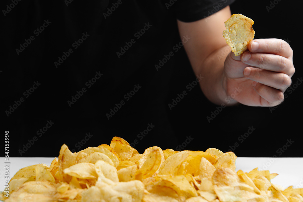 The man is eating junk food, chips on a dark background. Harmful food ...