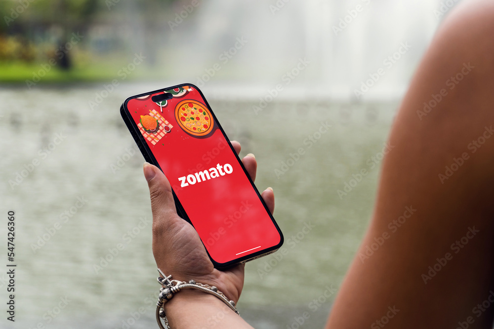Girl in the park holding a smartphone iPhone 14 Pro with Zomato ...