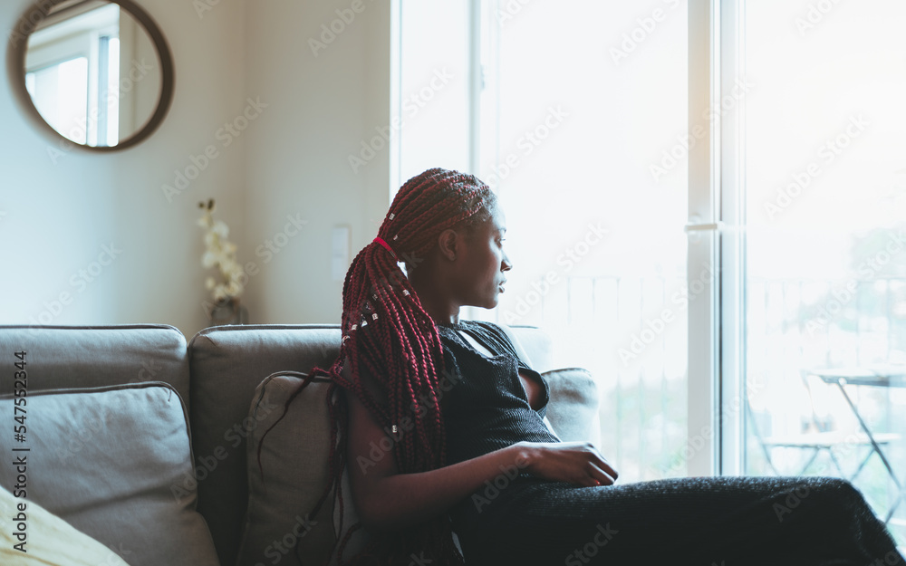 A pensive young African woman in a black dress and with long red box ...