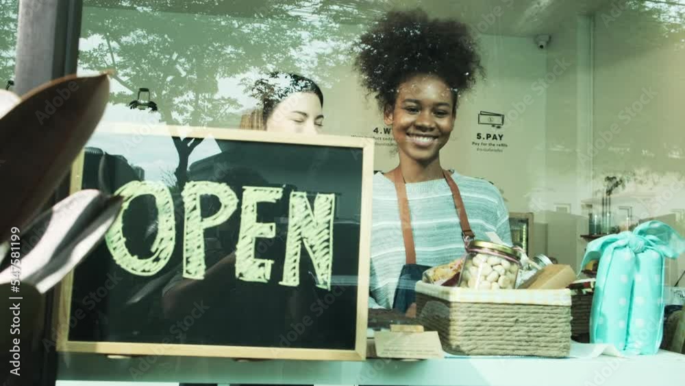 Two young female shopkeepers place open sign board at glass windows ...