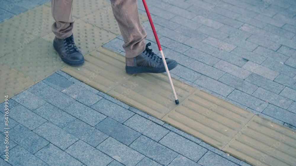 Visually impaired man is walking on a tactile warning tile with the ...