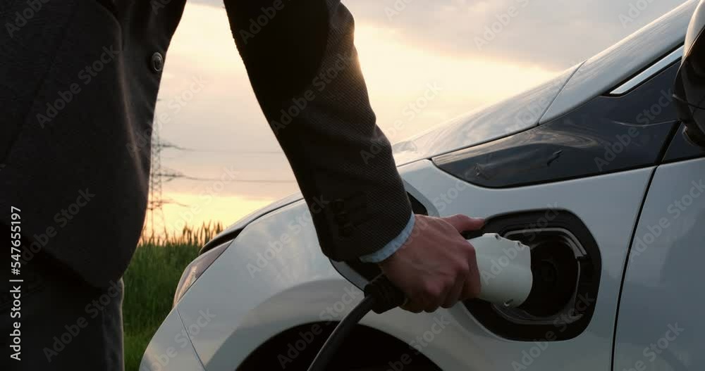 A man's hand connects the charging plug to an electric car in an open ...