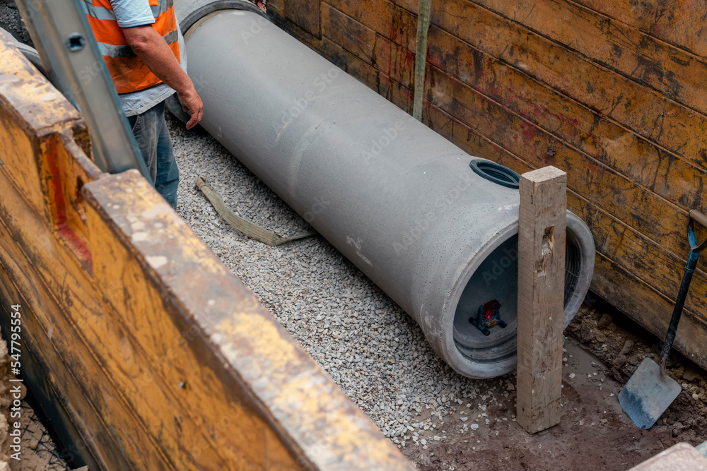 Builder installing big diameter concrete drainage pipe protected by ...