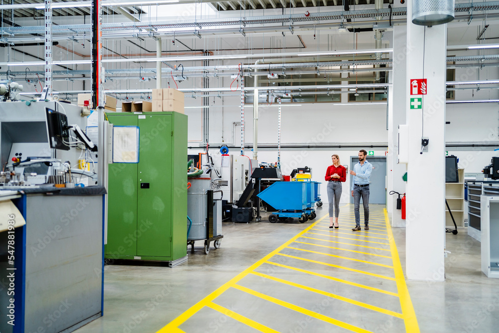 Business colleagues walking together on markings in production hall at ...