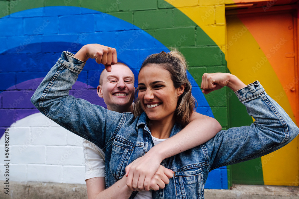 Non-binary person hugging lesbian woman flexing muscles in front of ...