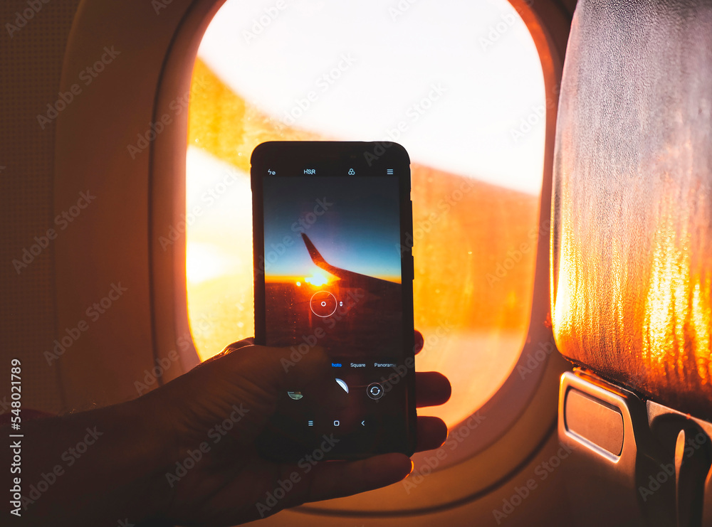 Taking photo of sunset from an airplane window. Hand holding phone ...