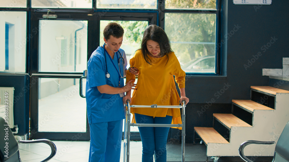 Female nurse helping patient with leg injury to use walk frame, dealing ...