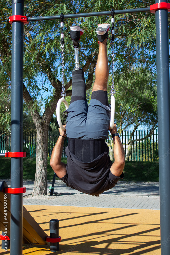 Back view of man with leg prothesis training on gymnastic rings ...