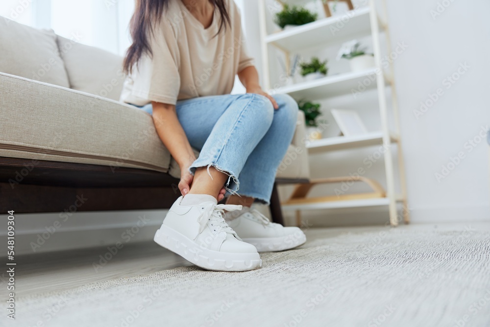 Woman sitting on the couch at home leg and foot pain, sprain and muscle ...