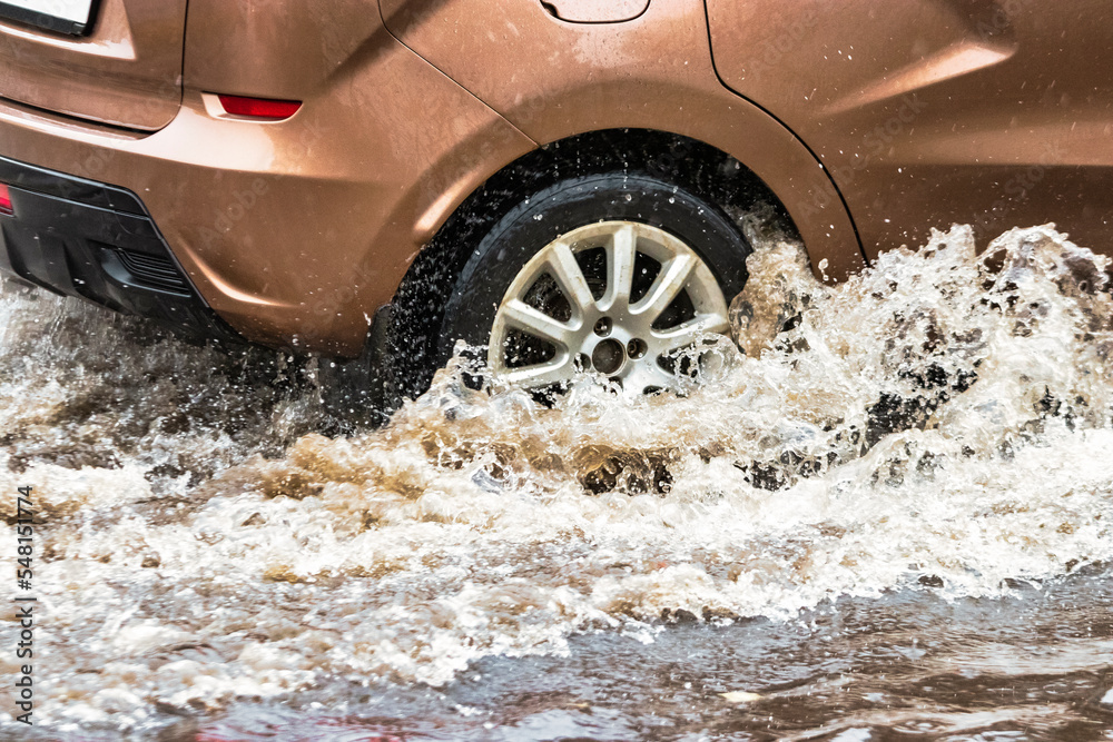 The car is driving through a puddle in heavy rain. Splashes of water ...