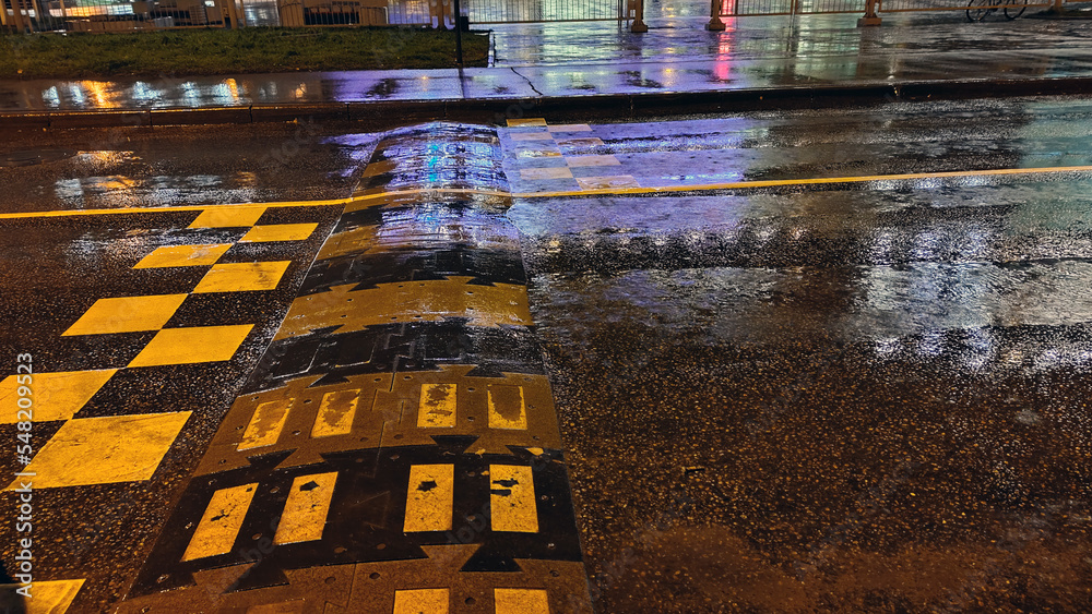Speed bump on wet pavement. Autumn rainy evening, yellow-black speed ...