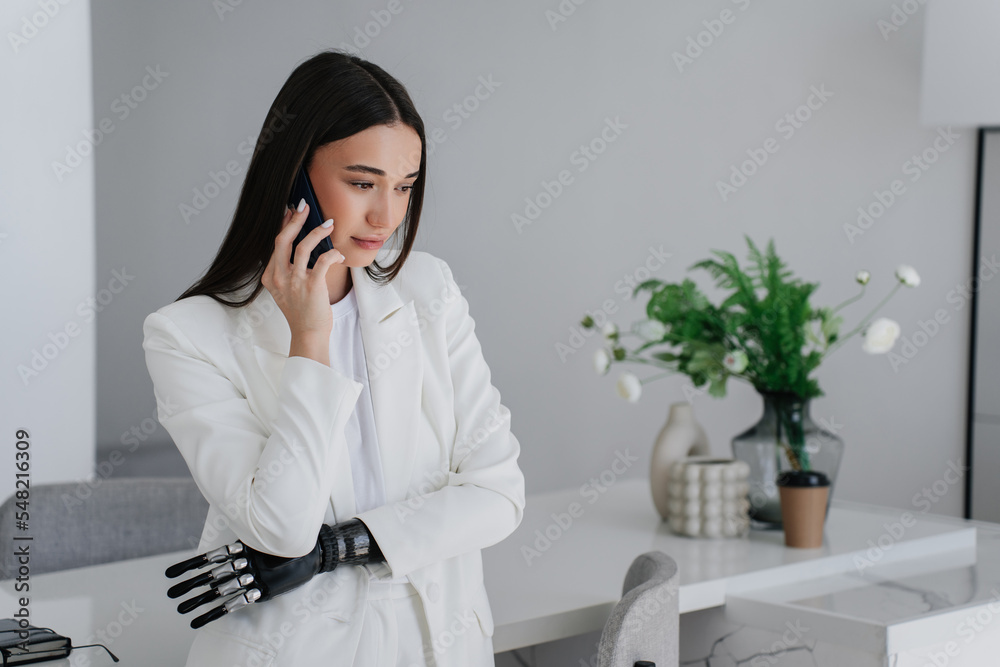 Calm gorgeous brunette girl with bionic hand talks by phone, smiling ...