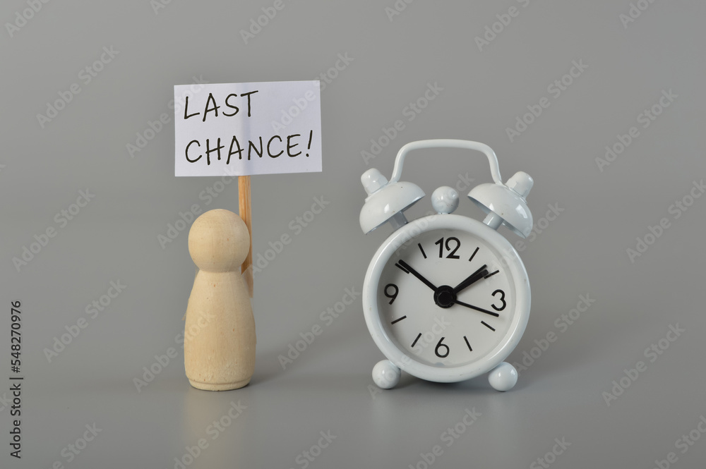 White clock and wooden doll figure hold sign board with text LAST ...