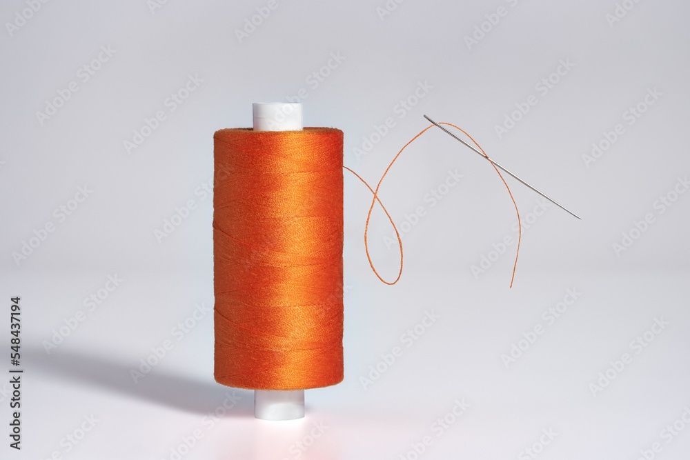 Spool of orange threads with a needle levitate on white background ...