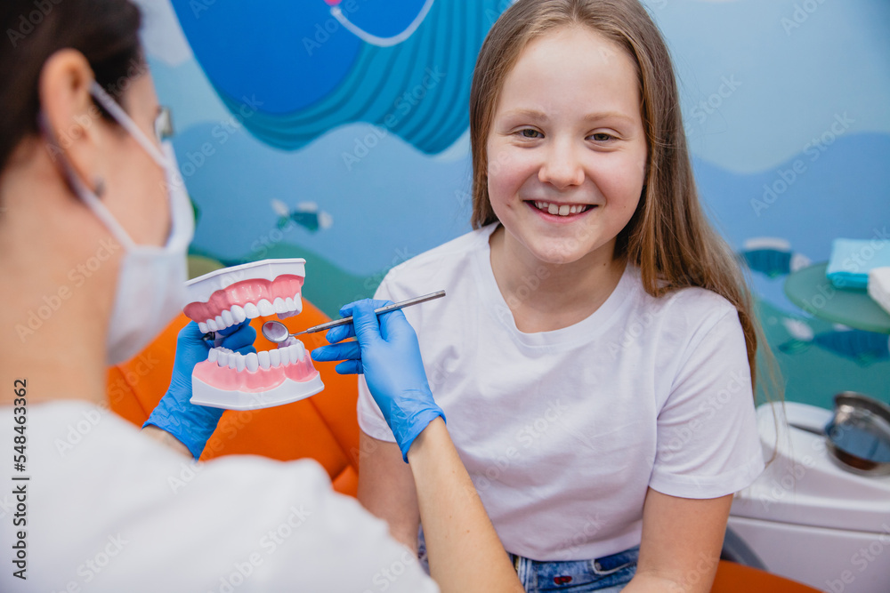 A female dentist shows a smiling girl of European appearance 10 years ...