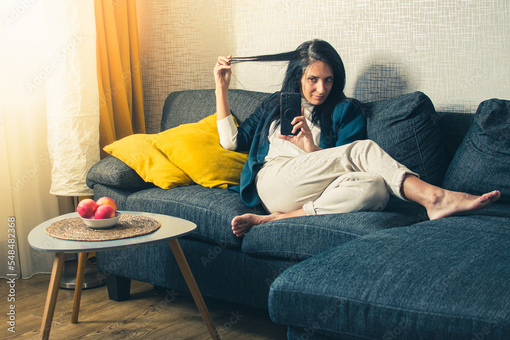 Beautiful young woman examining her scalp and hair in front of phone ...