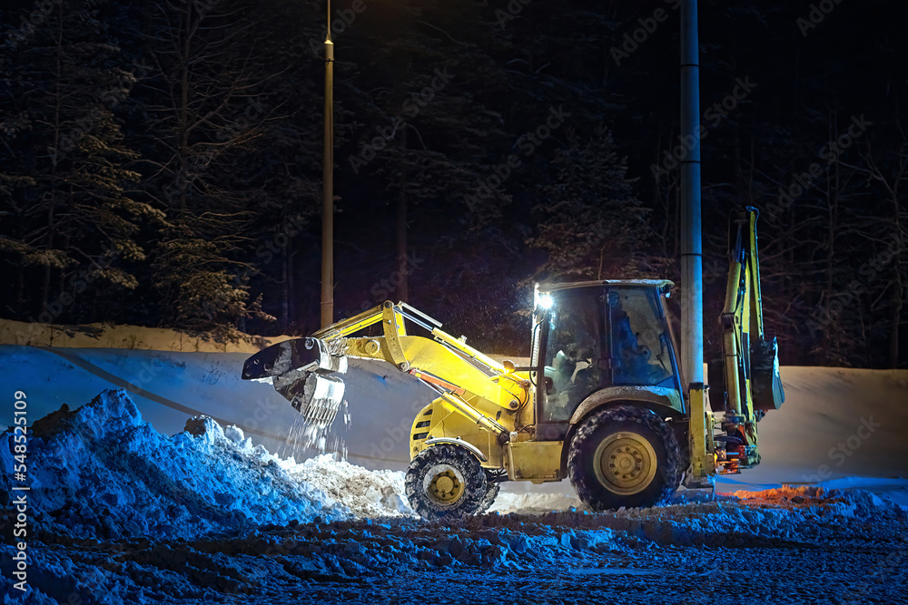 Backhoe loader cleans snow on parking lot outside the city, night snow ...