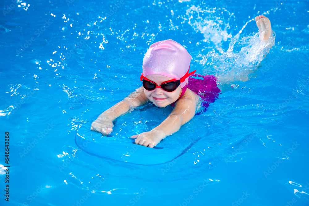 Preschool cute girl learning to swim in indoor pool with flutter board ...