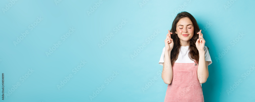 Portrait of cute and dreamy hopeful girl, close eyes and cross fingers ...