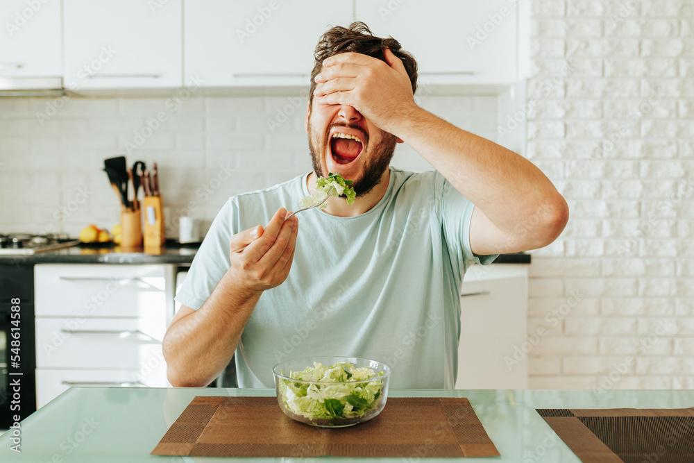 Front view young man man sits with a fork of salad and closes his eyes ...