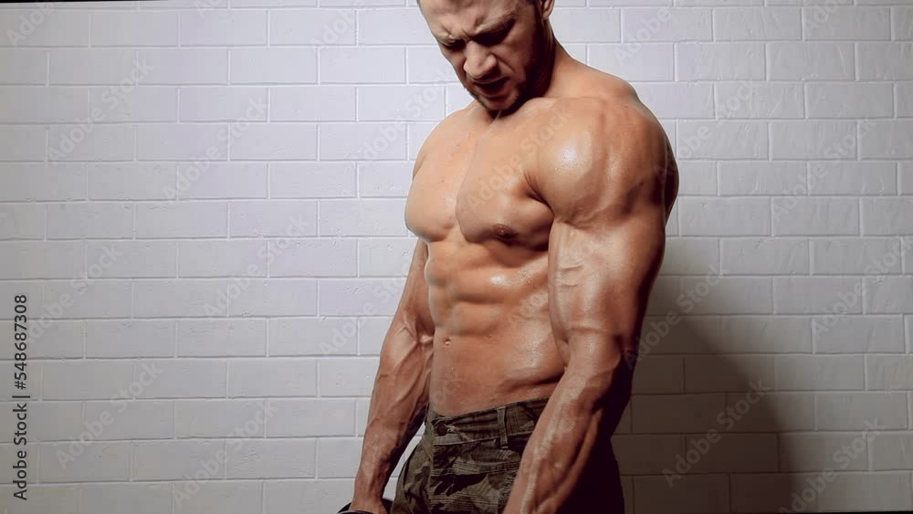 Side view of muscular topless bodybuilder who pumping biceps with ...