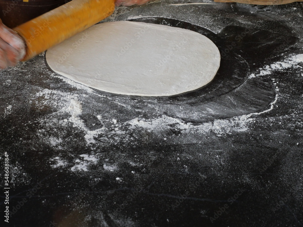 The chef's hand is rolling pizza dough into a flatten circle shape by ...