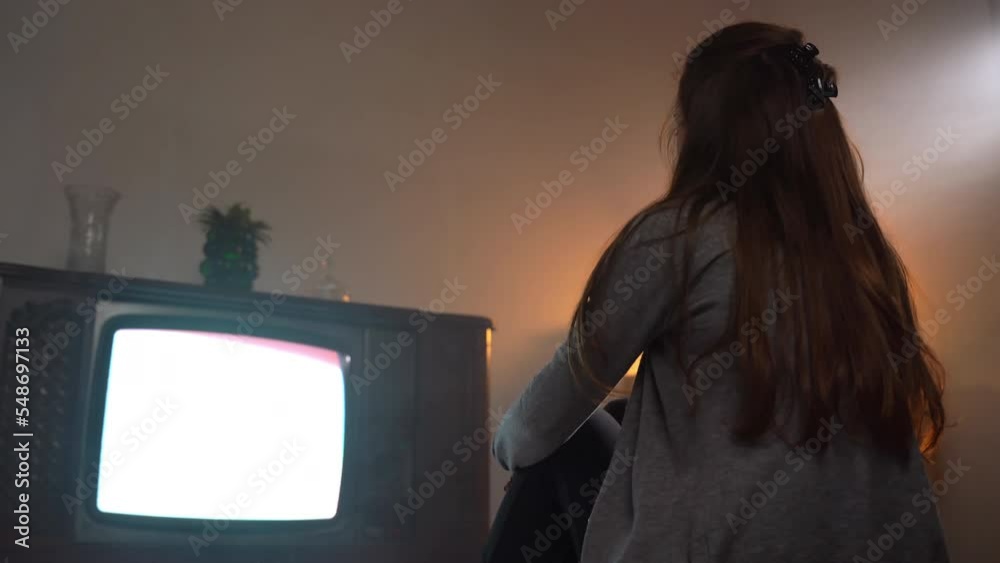 Broken vintage TV in dark illuminated room, woman sitting on the floor ...