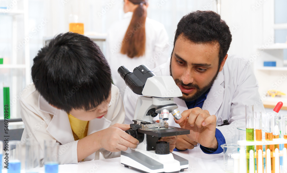 male teacher sitting at classroom desk with male student using ...