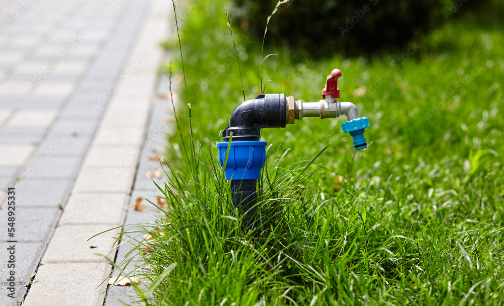 Faucet in a park to adjust water hose on it to hydrate the green grass ...