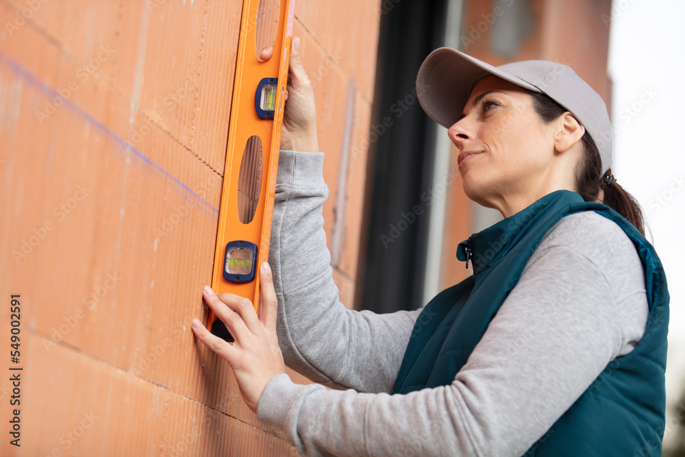 Foto de woman bricklayer holding a spirit level on a brick wall do ...