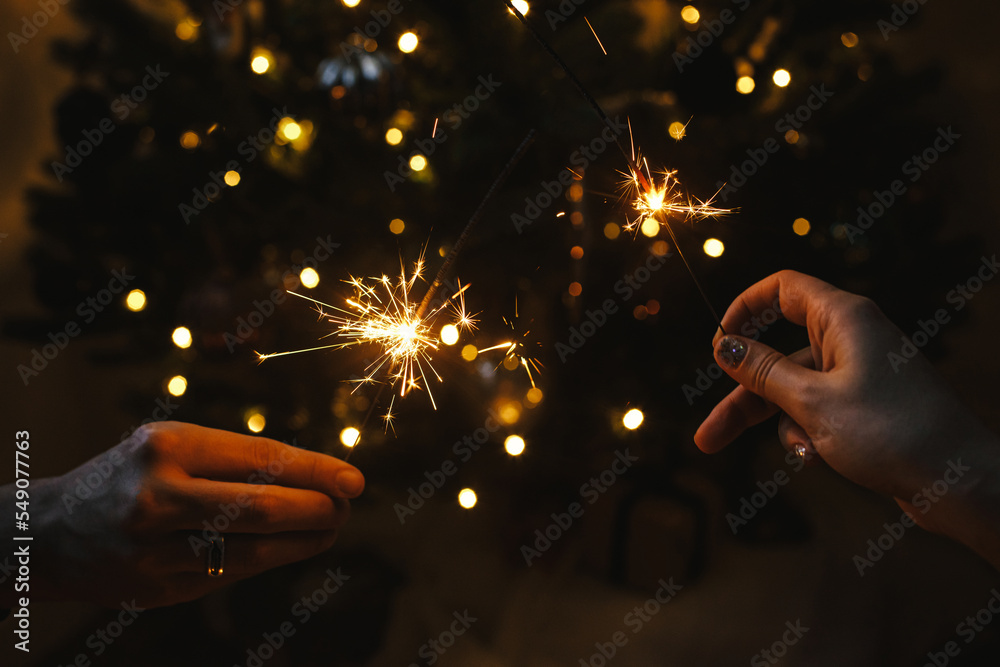 Hands holding firework against christmas tree lights in dark room ...