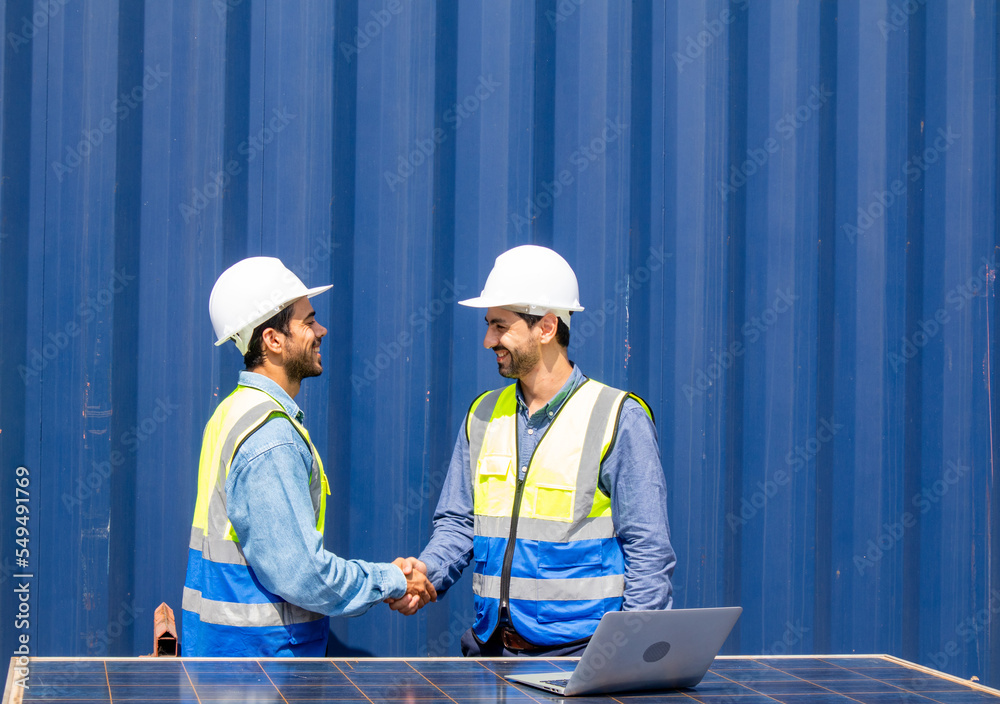 Two professional male engineers in helmets and uniforms shaking hands ...