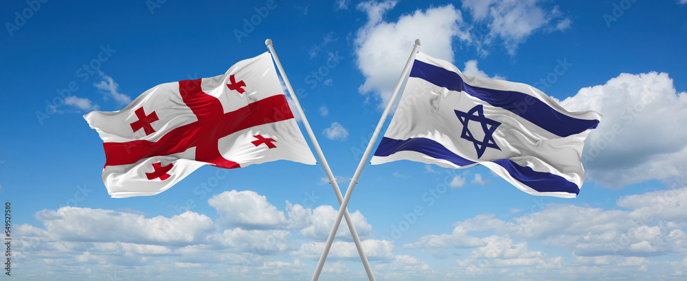 two crossed flags Israel and Georgia waving in wind at cloudy sky ...