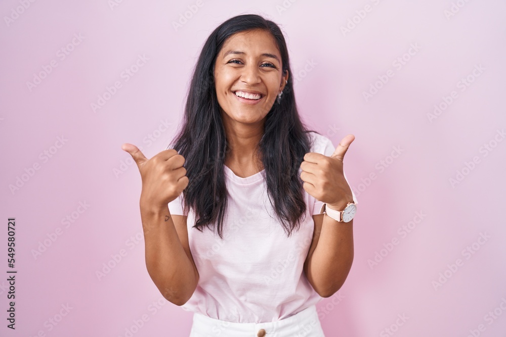 Young hispanic woman standing over pink background success sign doing ...