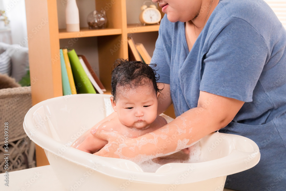 Asian newborn baby in bathtub taking a shower filled with soap bubbles ...