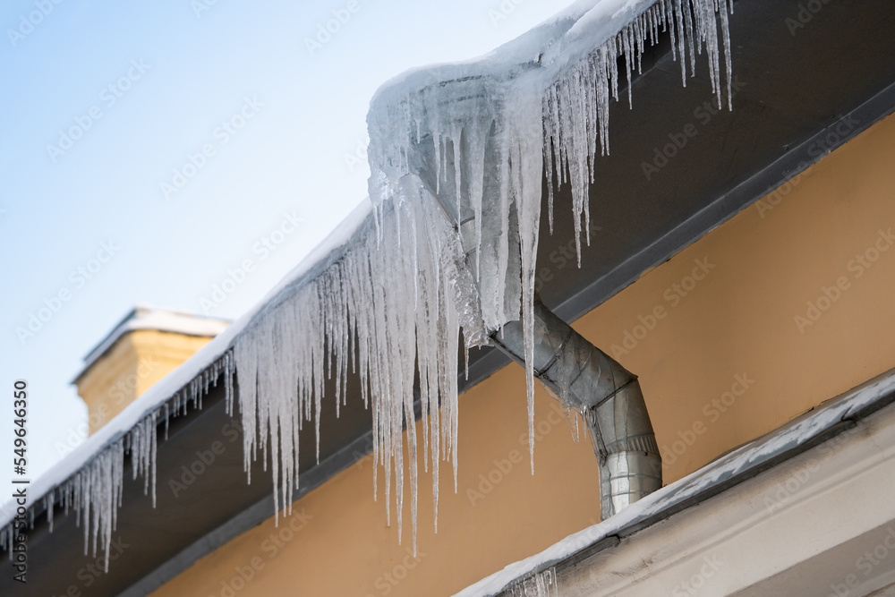 Big frozen icicles dangerously hanging from building edge on cold winter day, dangerous ice ...