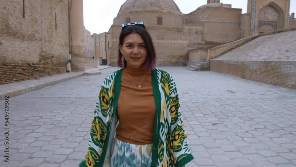An oriental girl in a traditional Uzbek dress walks along an old Muslim ...