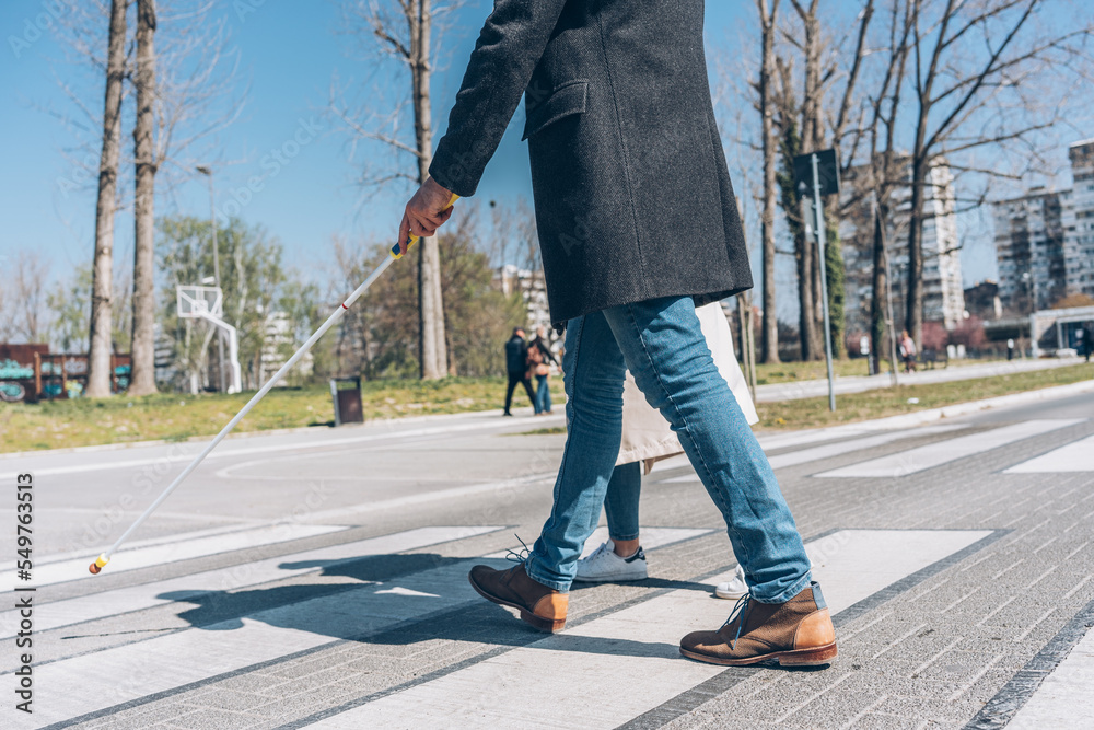 A blind male person using a white cane and walks with his female friend ...