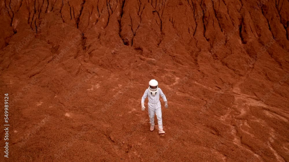 Astronaut walking on red planet surface to the aerial camera. Dronnie ...